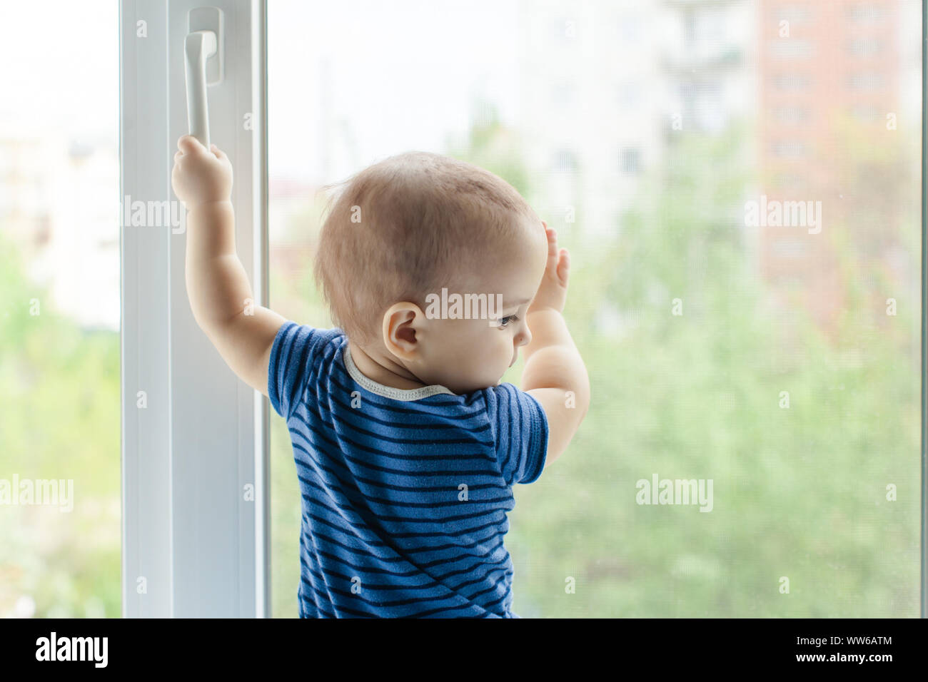 Baby boy sit on the windowsill and trying to open the window pulling ...