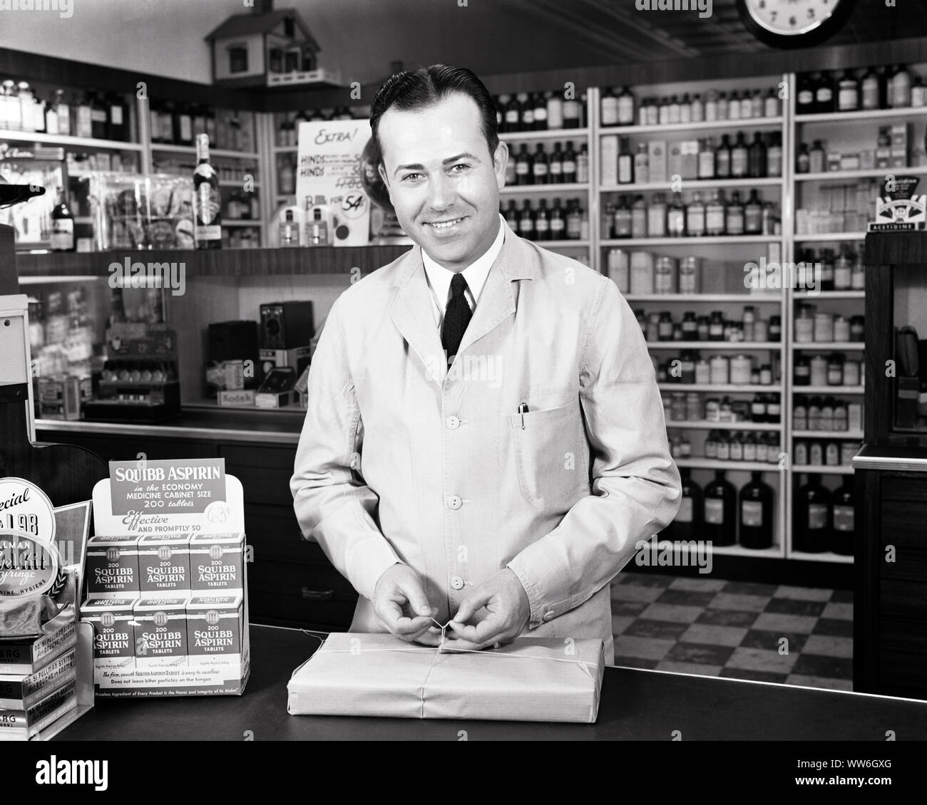 1930s SMILING MAN BEHIND COUNTER AT PHARMACY WRAPPING PACKAGE IN BROWN ...