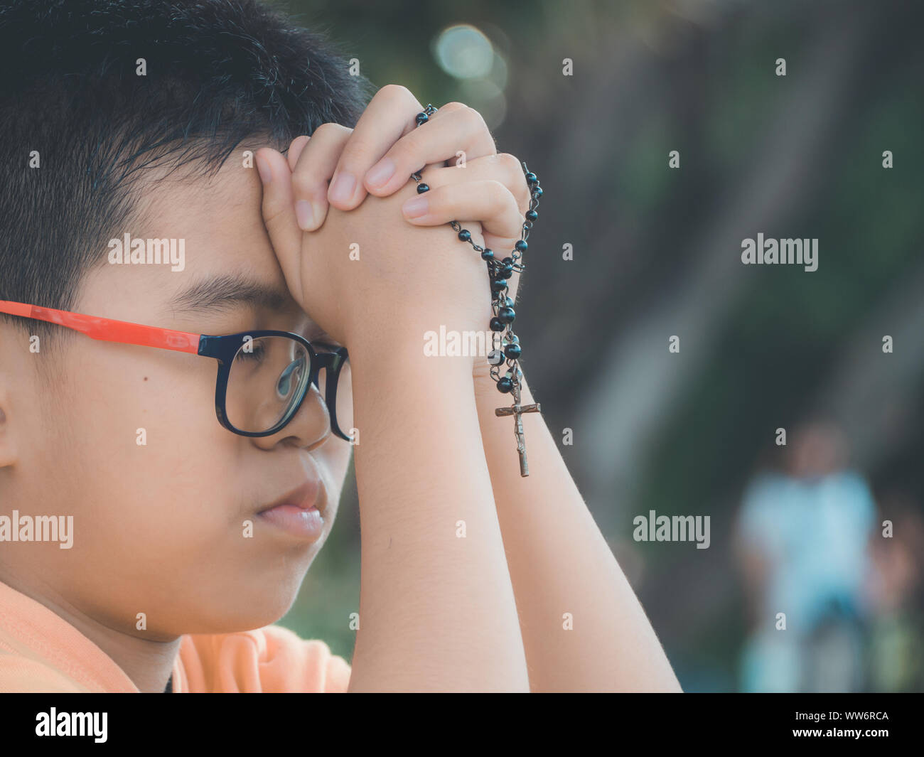 Religious young boy praying hands with the cross to God at park Stock ...