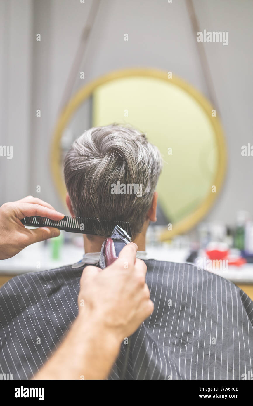 Rear view of professional barber styling hair of his client by using ...