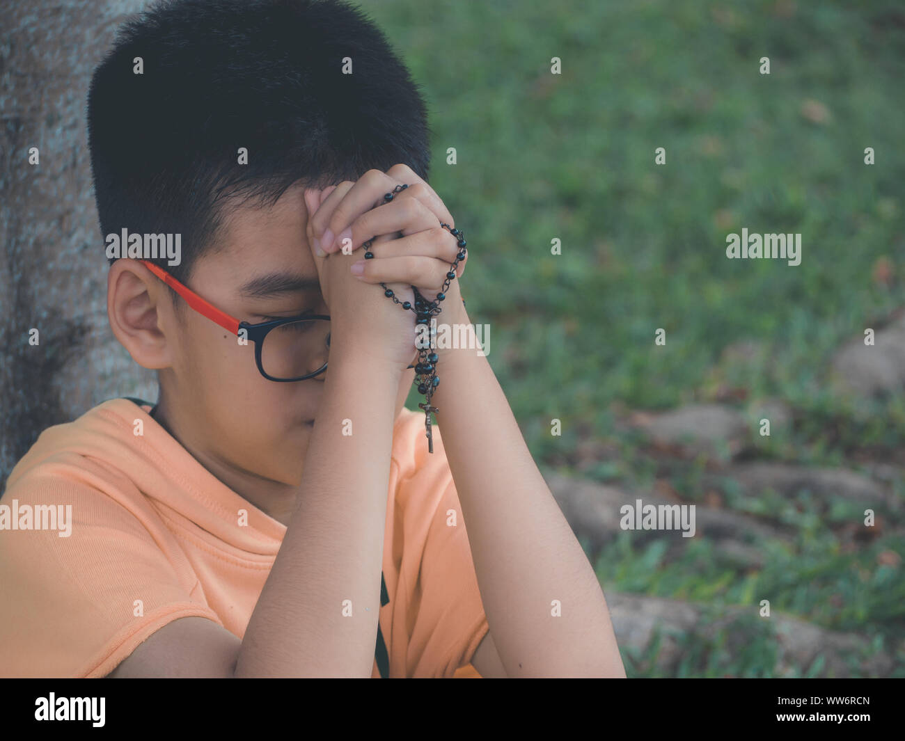 Religious young boy praying hands with the cross to God at park Stock ...