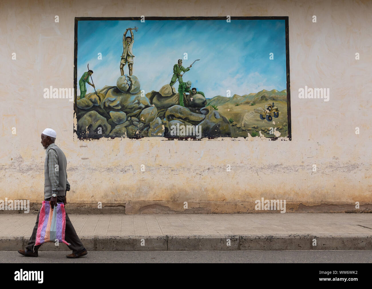 Eritrean man pssing in front of a propaganda mural about the war with ...