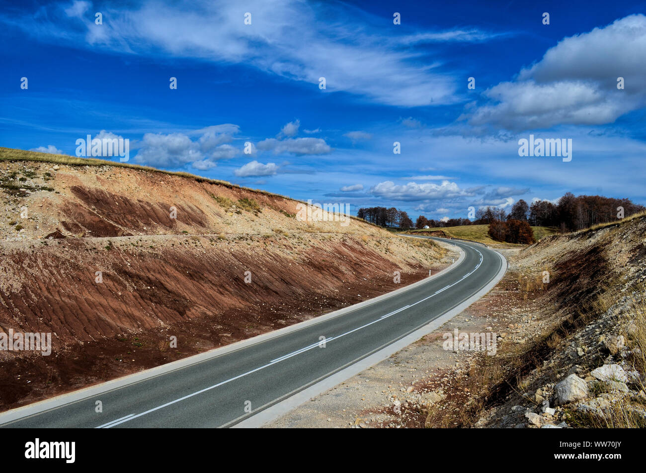Mountain asphalt road, cut through red ground, band ind the road and ...