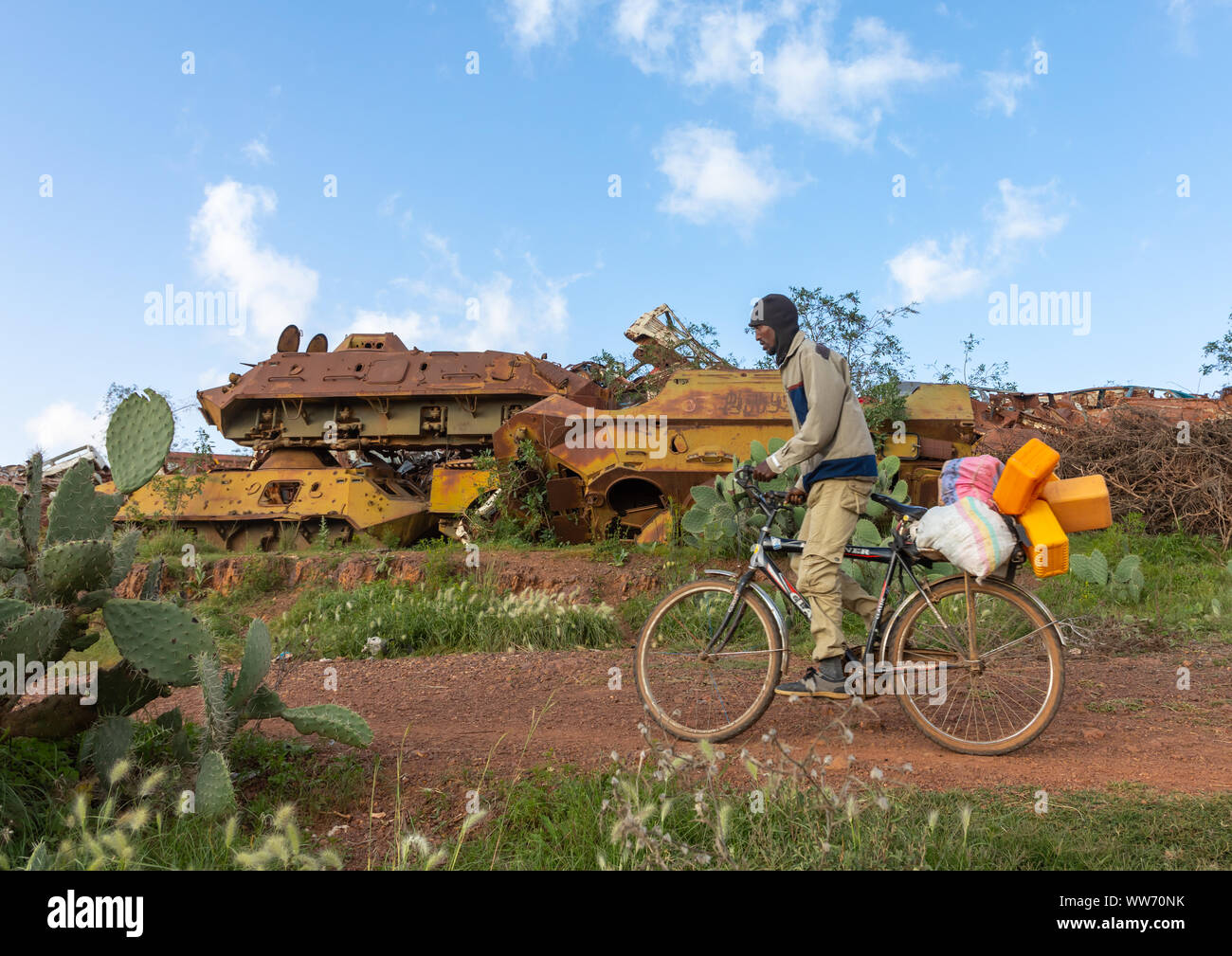Eritrean man riding a bicycle in front of the military tank graveyard ...