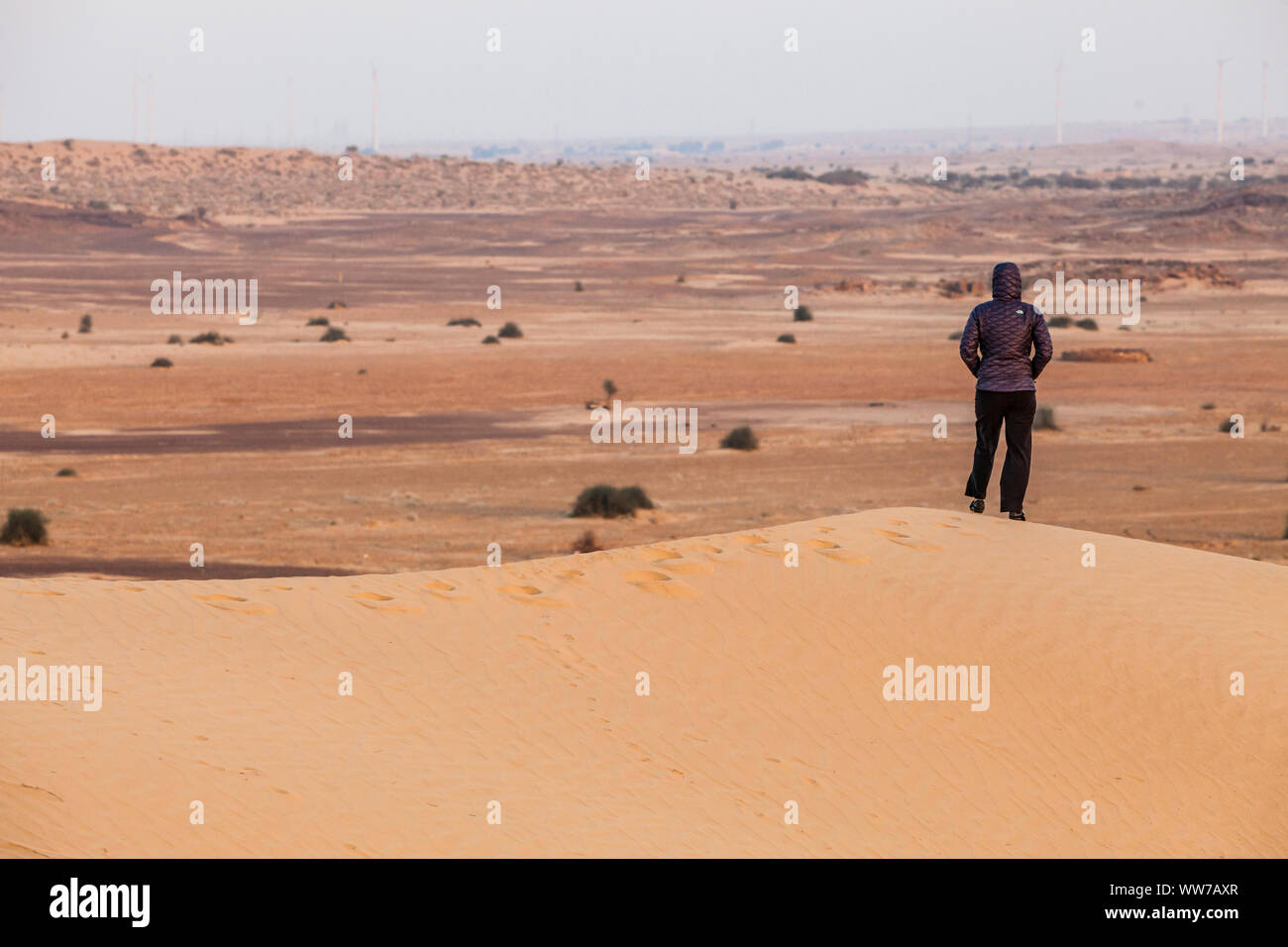 A female tourist stands atop a sand dune watching the sunrise over the ...
