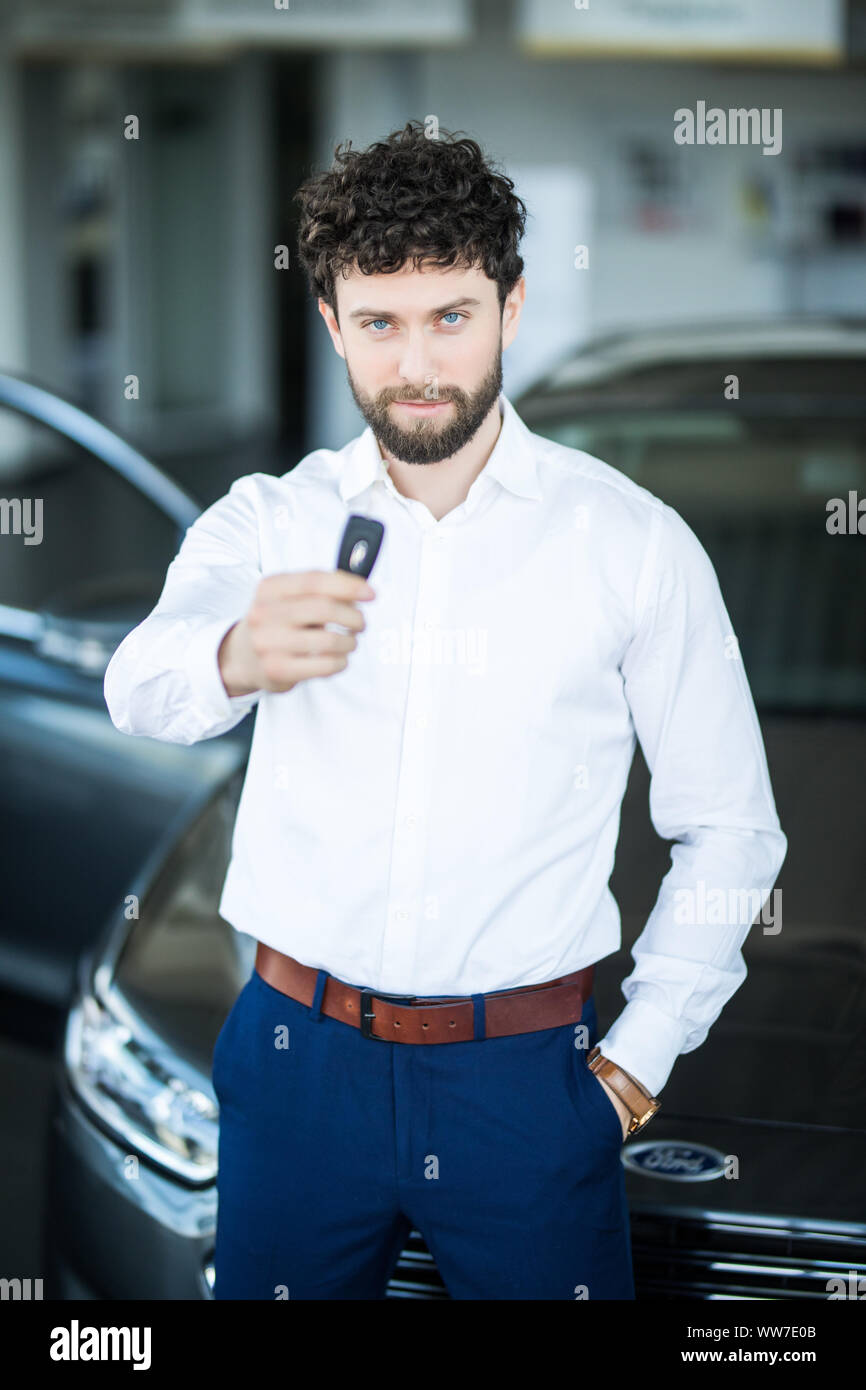 Car salesman in car dealership with key presenting his new and used ...
