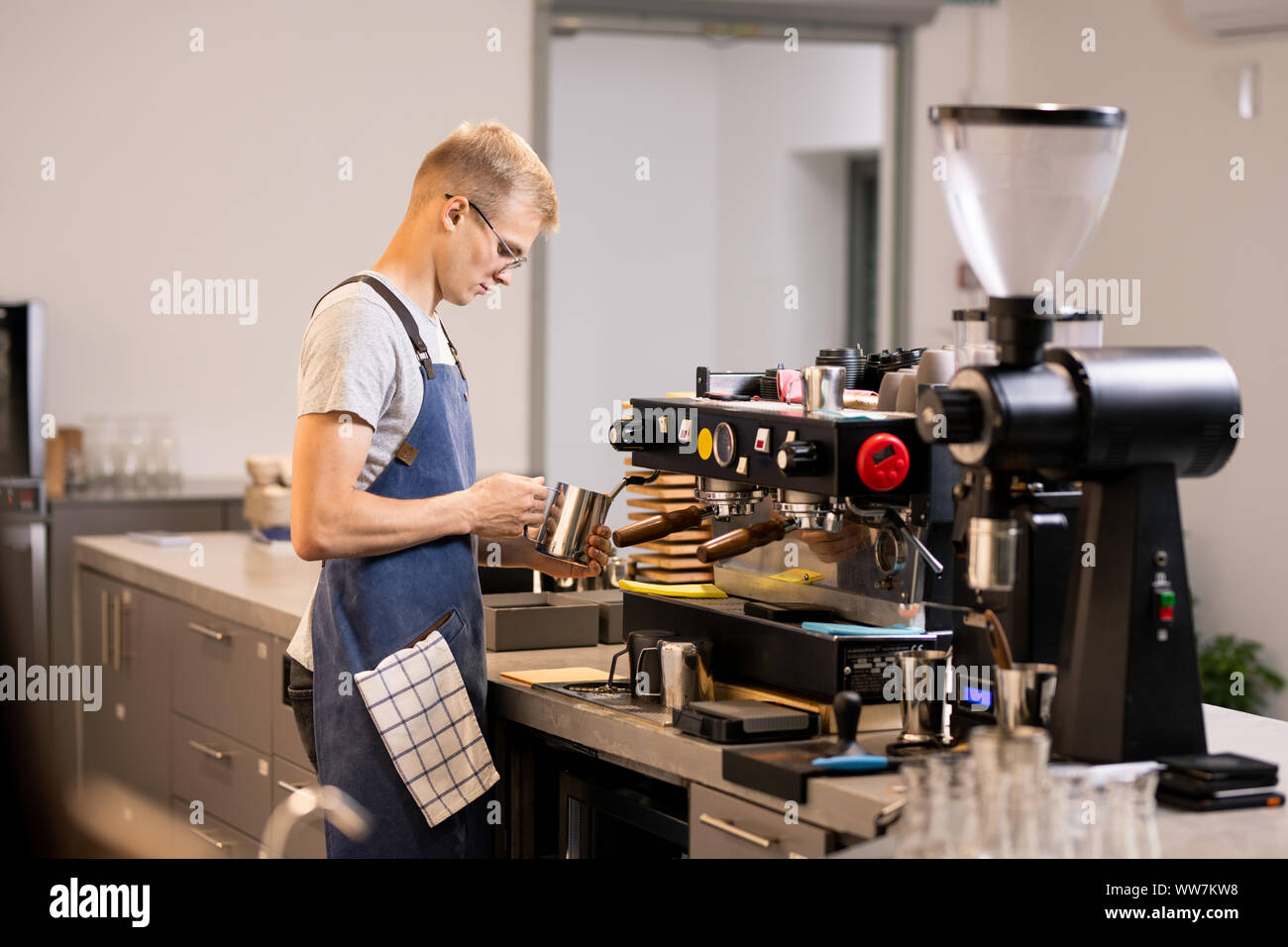 Young barista standing by coffee machine while preparing drinks for ...
