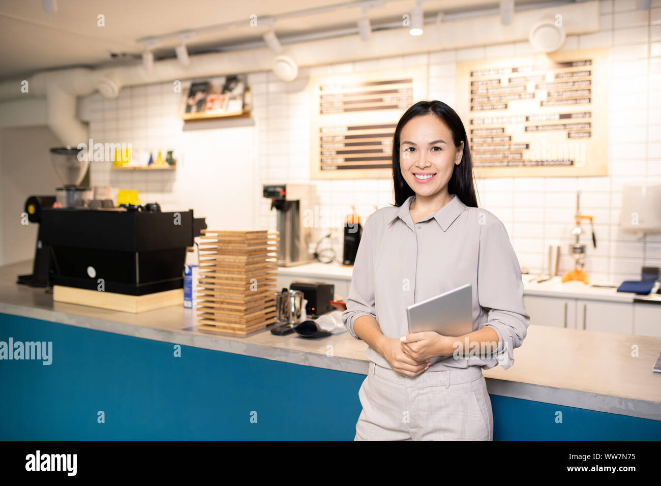 Happy young brunette waitress standing by counter and waiting for you ...
