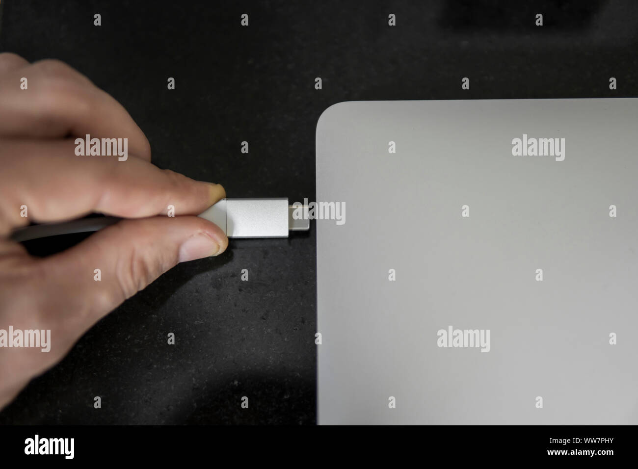 Male hand plugging white USB-C Type C cable into a port on a grey ...