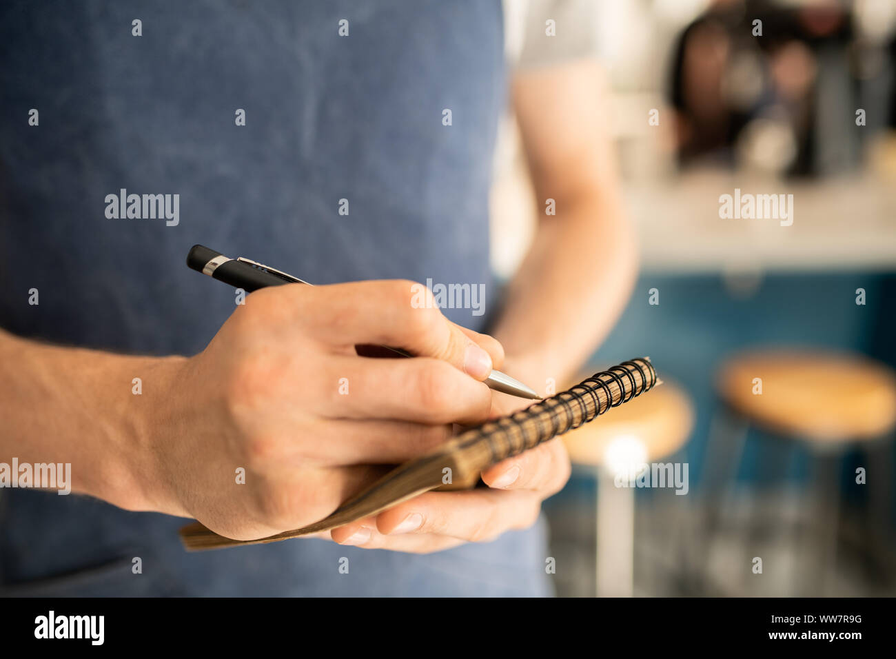 Hand of waiter in apron holding ballpoint over page of notepad while ...