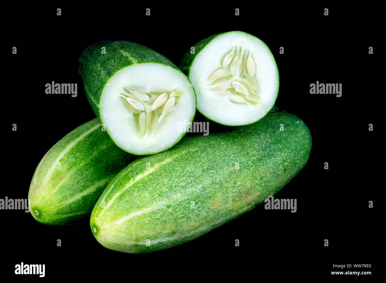 Whole and cut organic cucumbers isolated against a black background ...