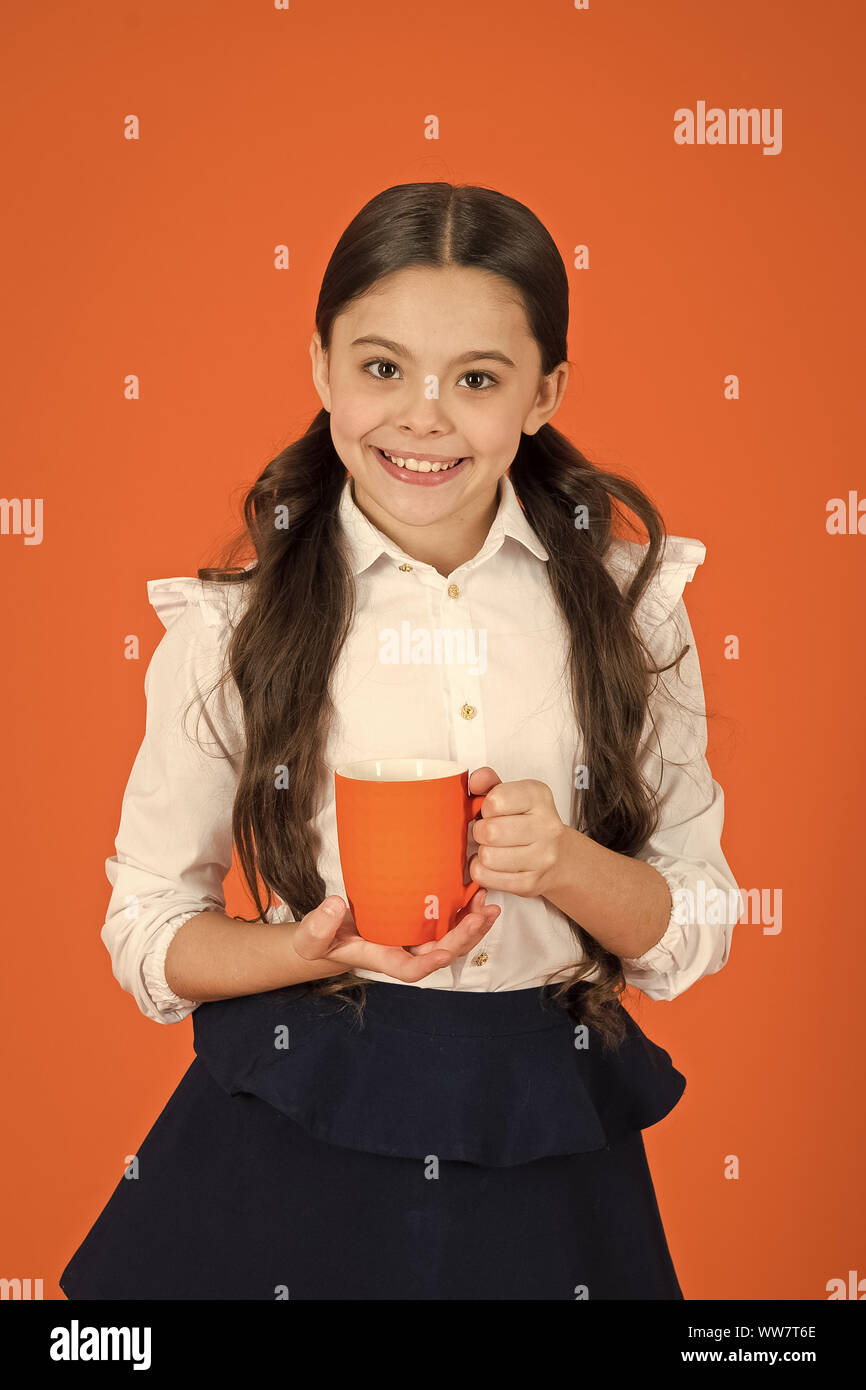 Girl kid school uniform orange background. Schoolgirl hold mug. School ... Girl kid school uniform orange background. Schoolgirl hold mug. School ...