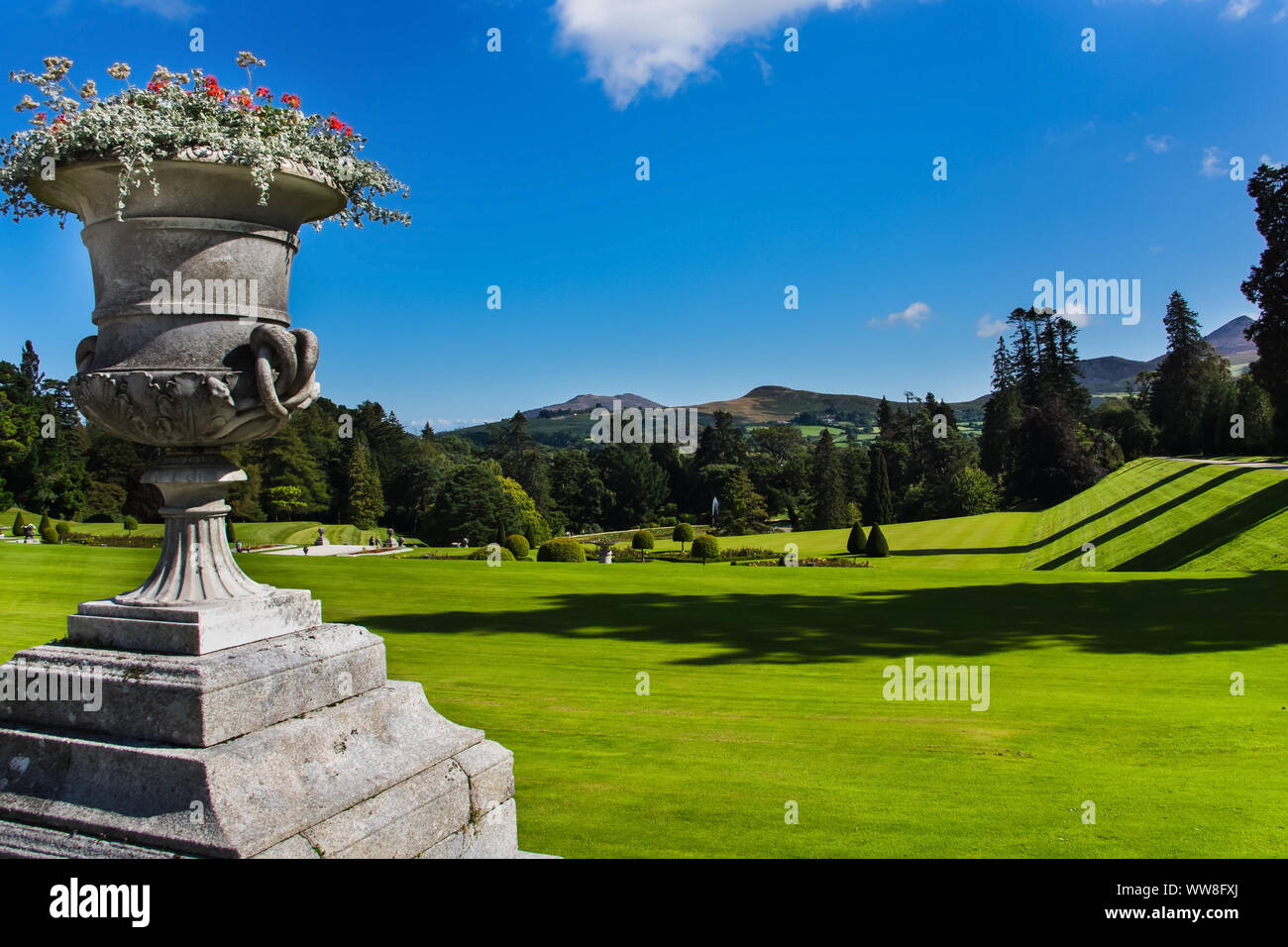 An ornate pot with flowers and wide green lawn in Powerscourt gardens ...