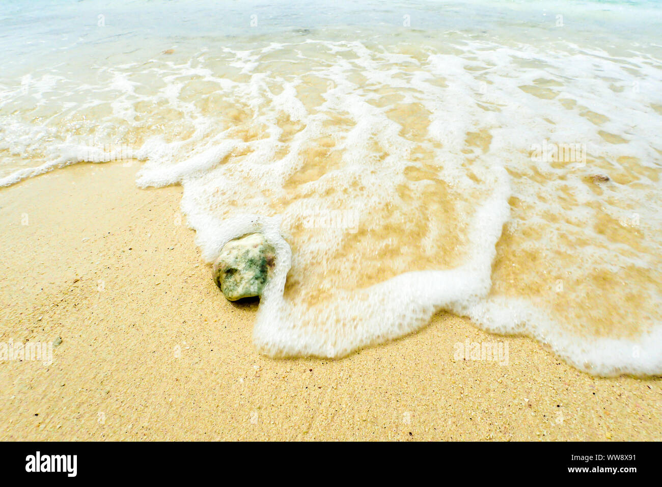 Ocean sea water rushing in to sandy beach shore on a cloudy blue sky ...