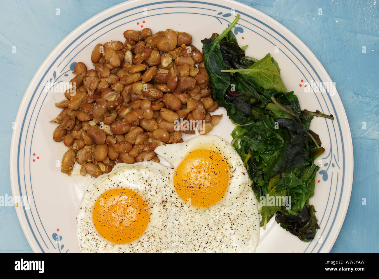 Breakfast of eggs, sunny side up, baked beans, and steamed greens Stock ...
