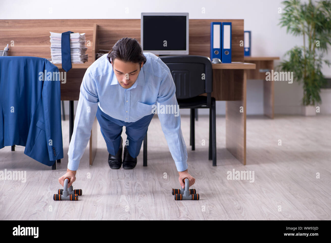 The young handsome businessman doing exercises at workplace Stock Photo ...