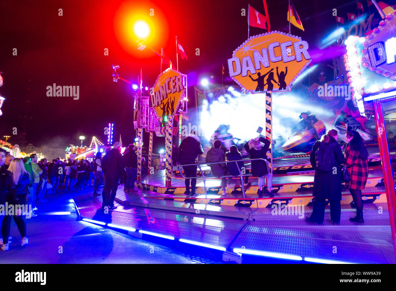 Teenagers watch the cars on a spinning fairground ride zip past them at ...