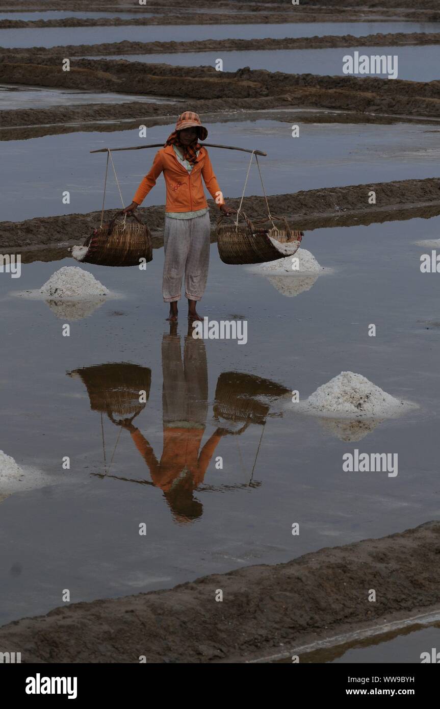 Reflection of a salt field worker carrying rattan baskets laden w ...