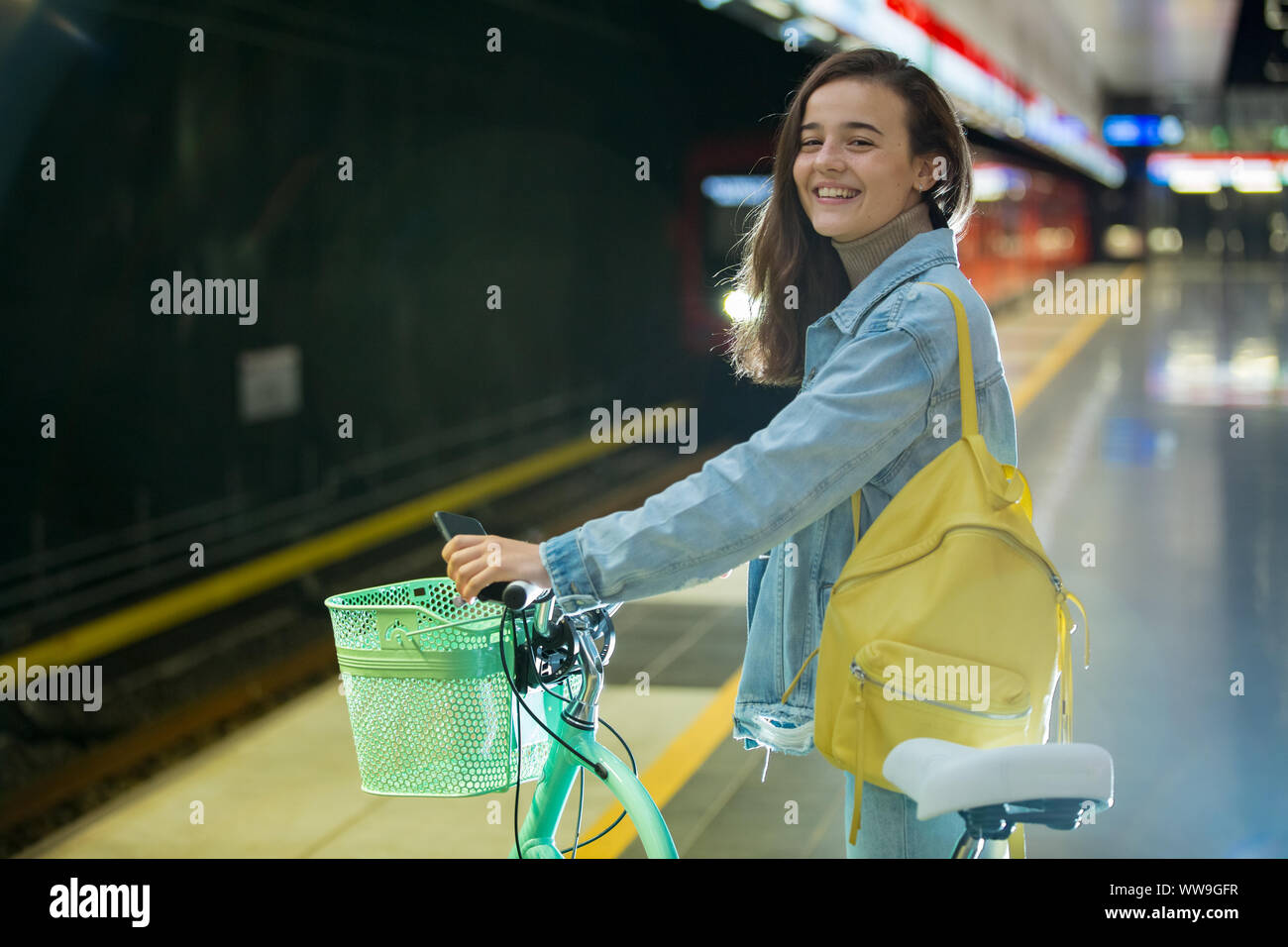 Teenager girl in jeans with yellow backpack and bike standing on metro ...