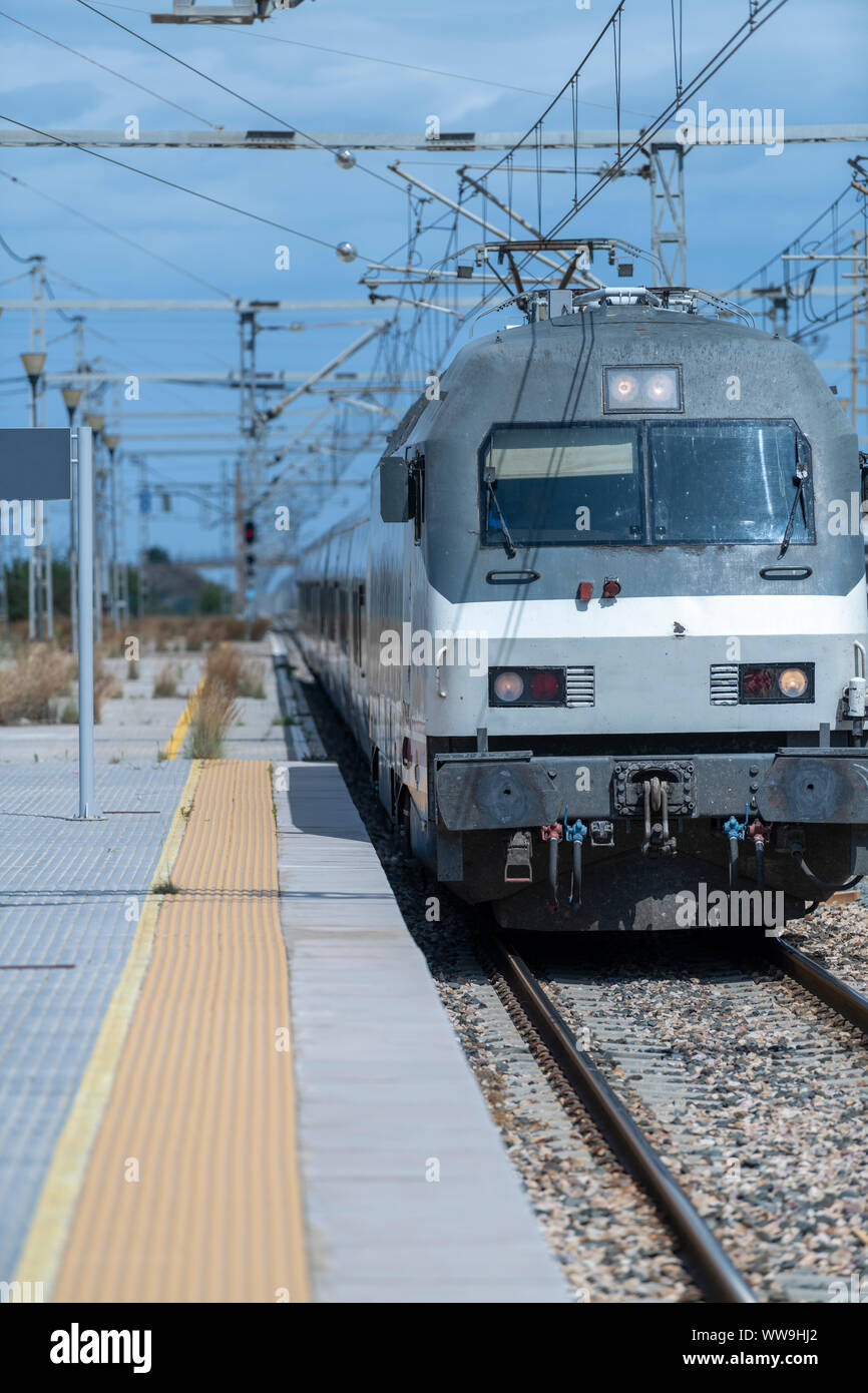 A grey and white train with wired metal posts and blue sky with white ...