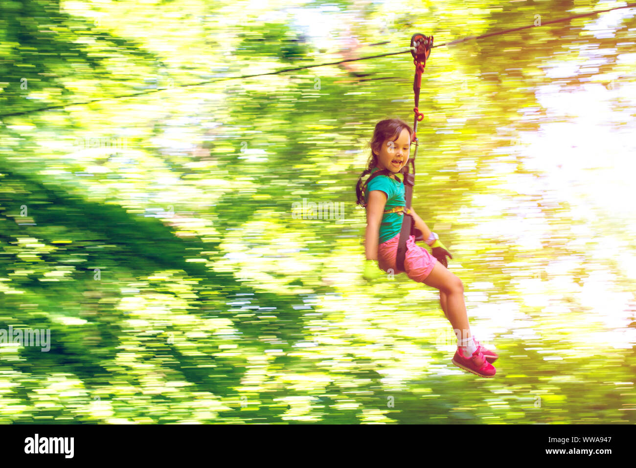 Happy little girl on zip line between trees, panning effect Stock Photo ...