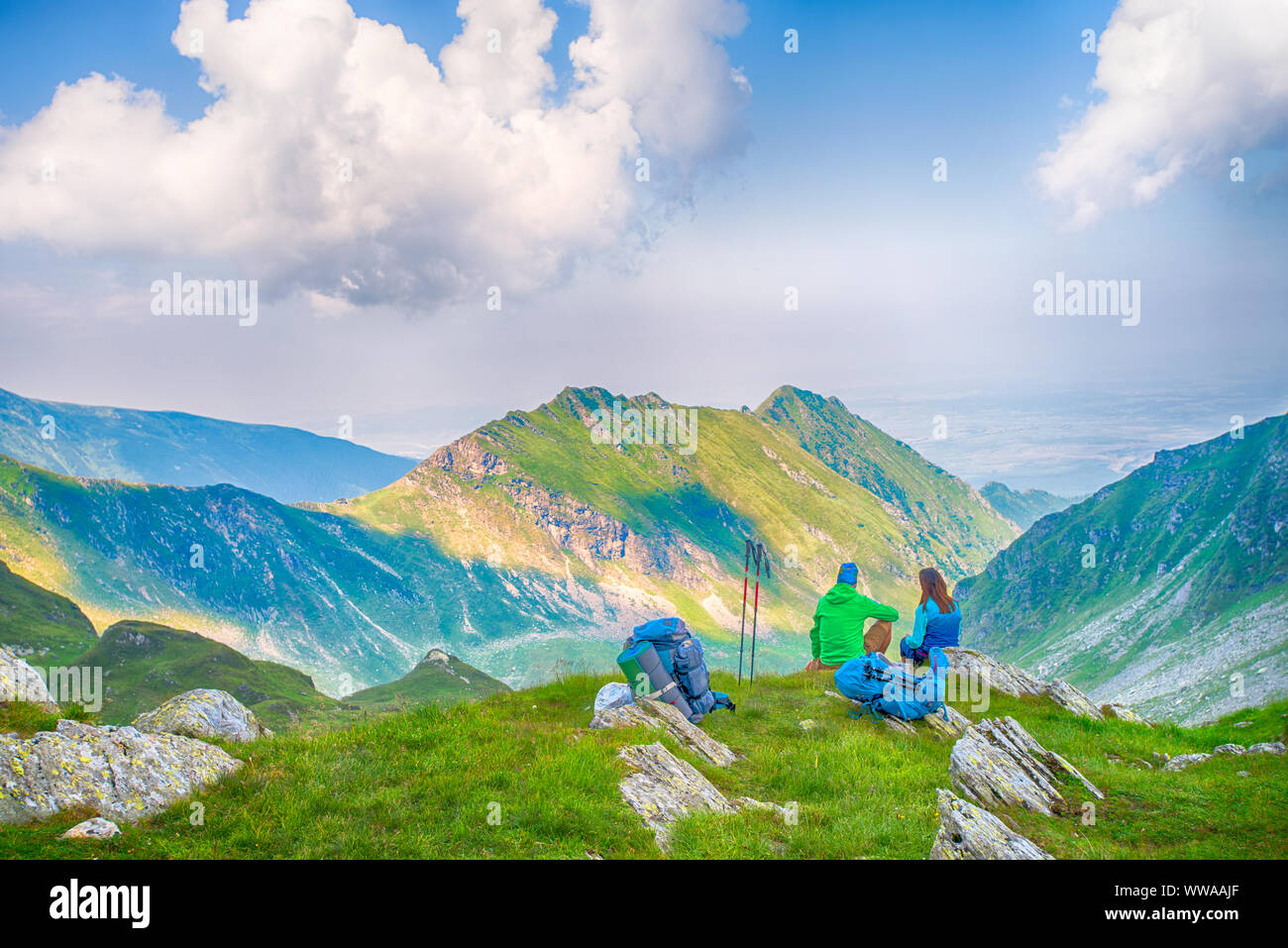Back shot of young couple sitting down in the mountains on edge of ...