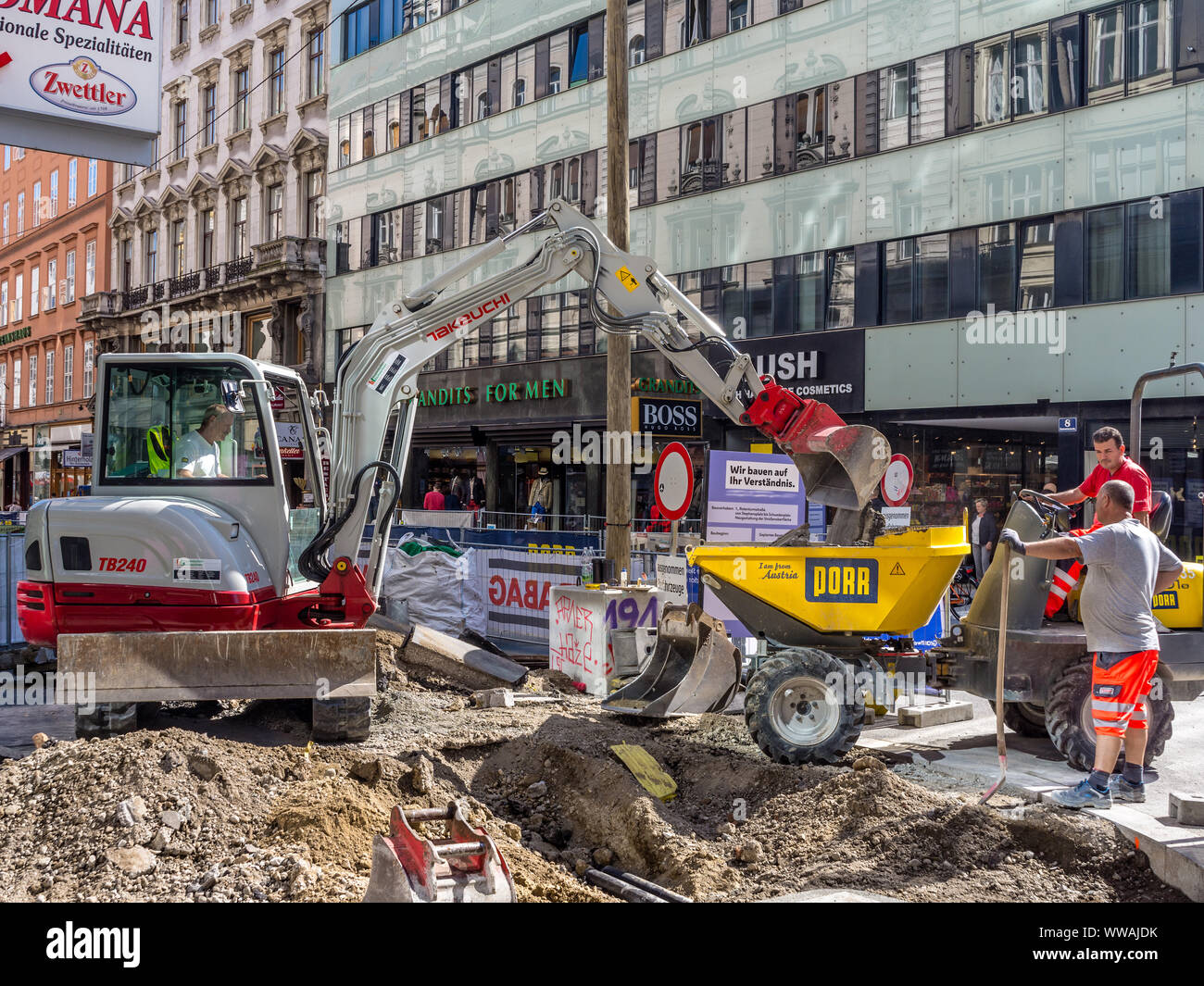 Workers using mechanical excavator to dig trench in city street ...