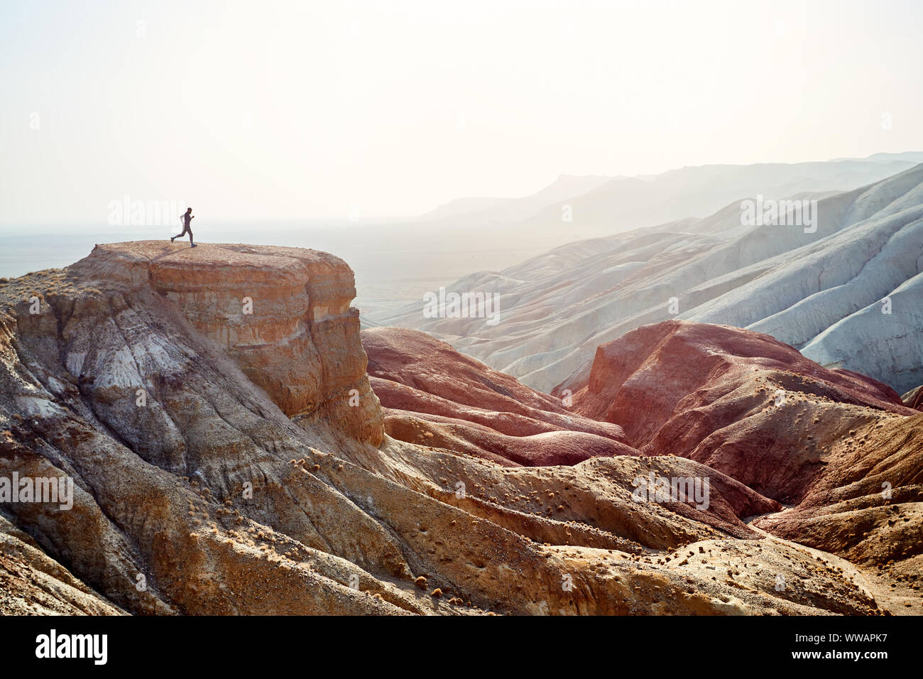 Silhouette of runner athlete on the big rock in canyon with red desert ...