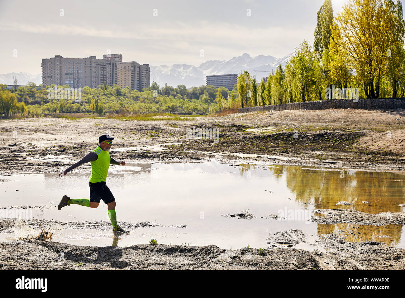 Man with grey beard running on the dirty trail with pool at mountain ...