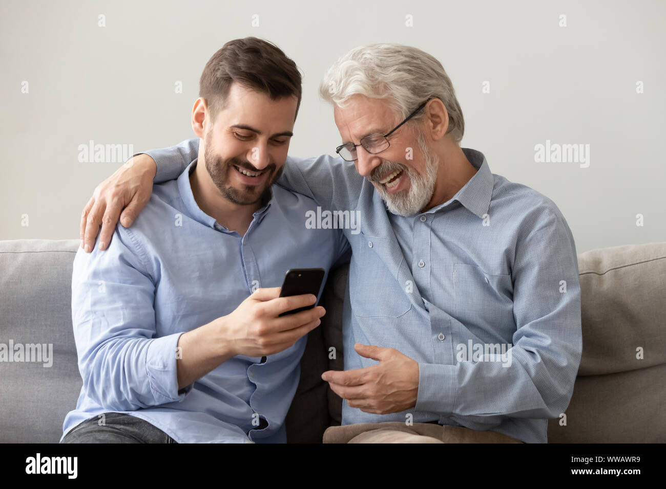 Happy family old father embracing young son enjoying using smartphone ...