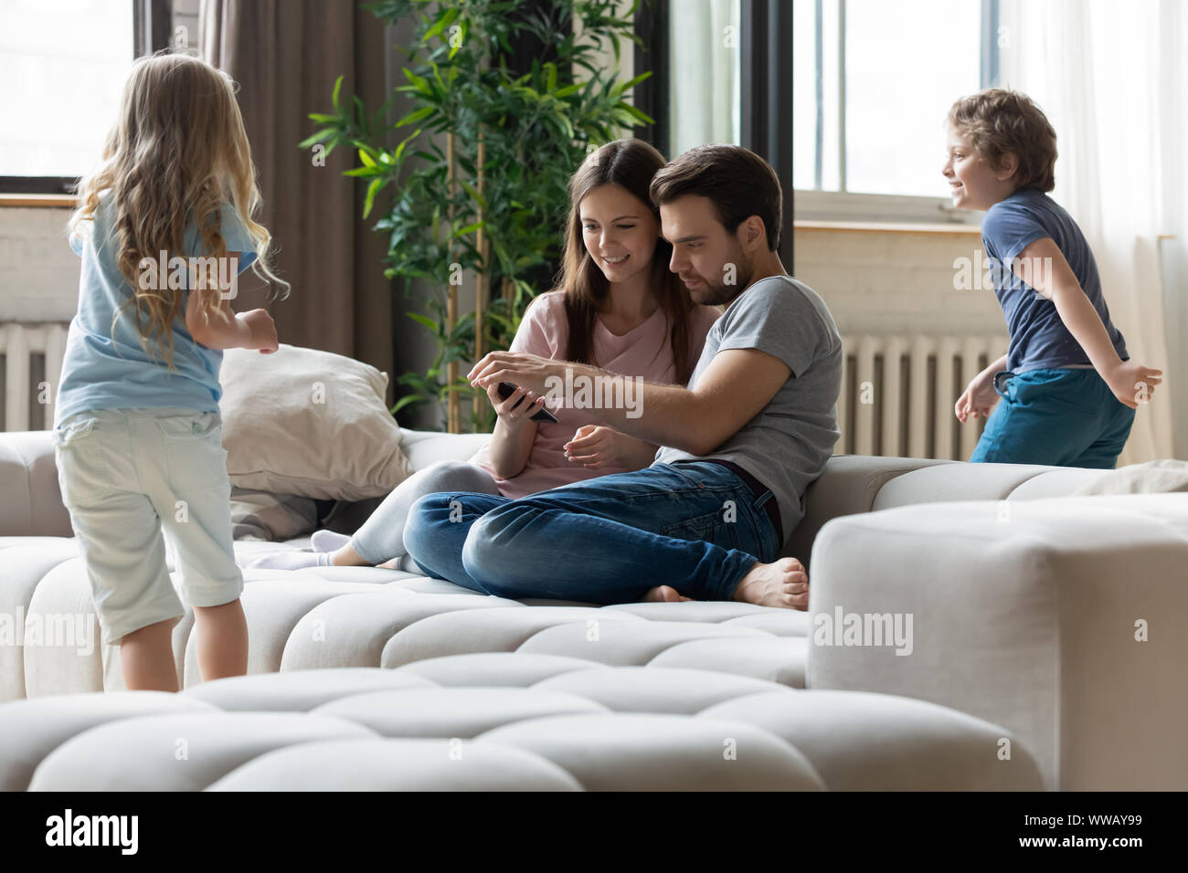 Smiling parents using phone while children running around Stock Photo ...