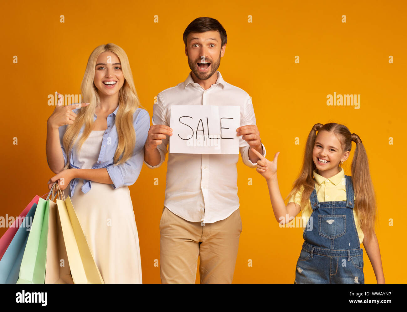 Family Pointing At Sale Sign Holding Shopping Bags, Studio Shot Stock ...