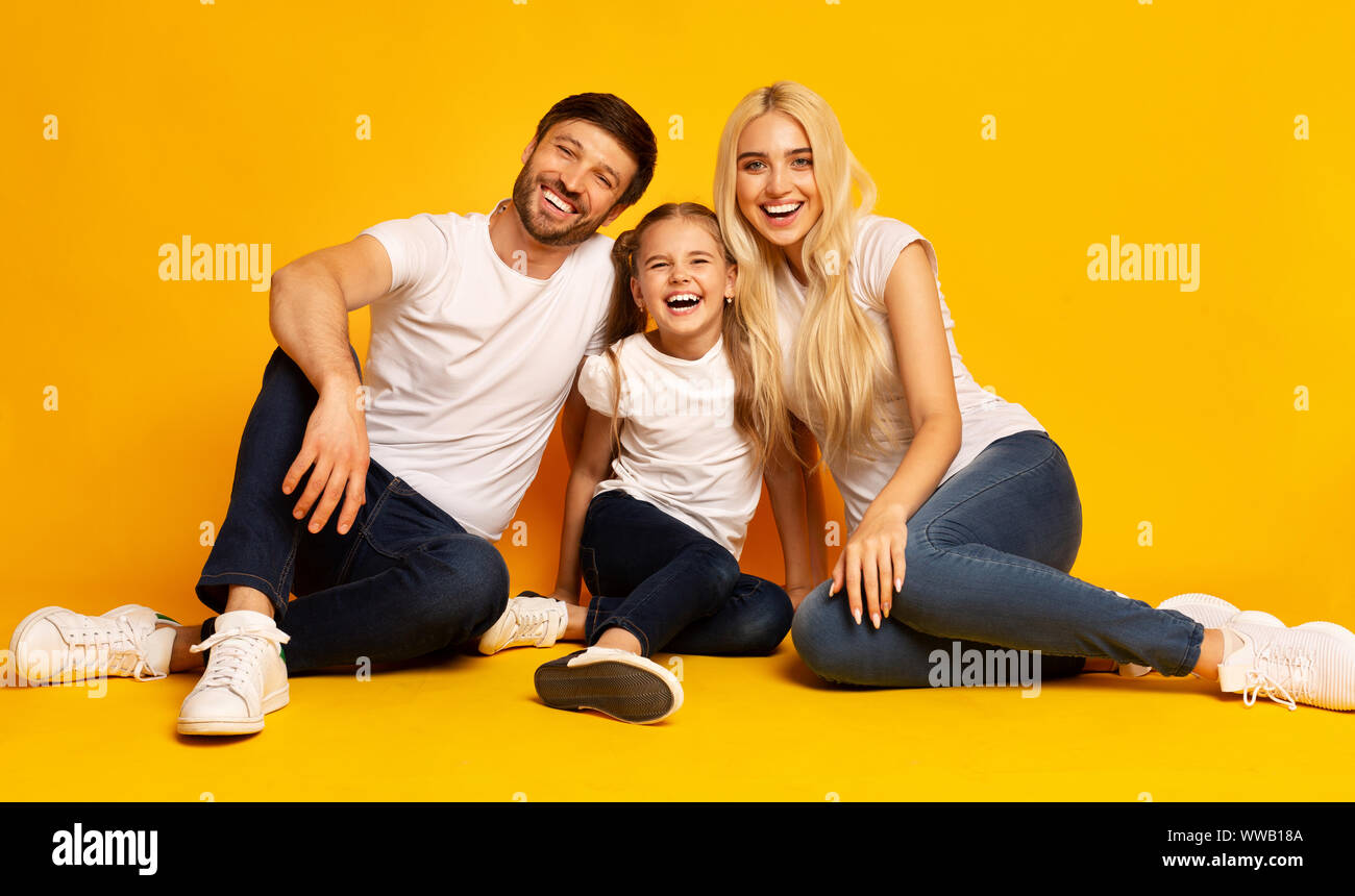 Family Of Three Sitting Together On Floor Over Yellow Background Stock ...