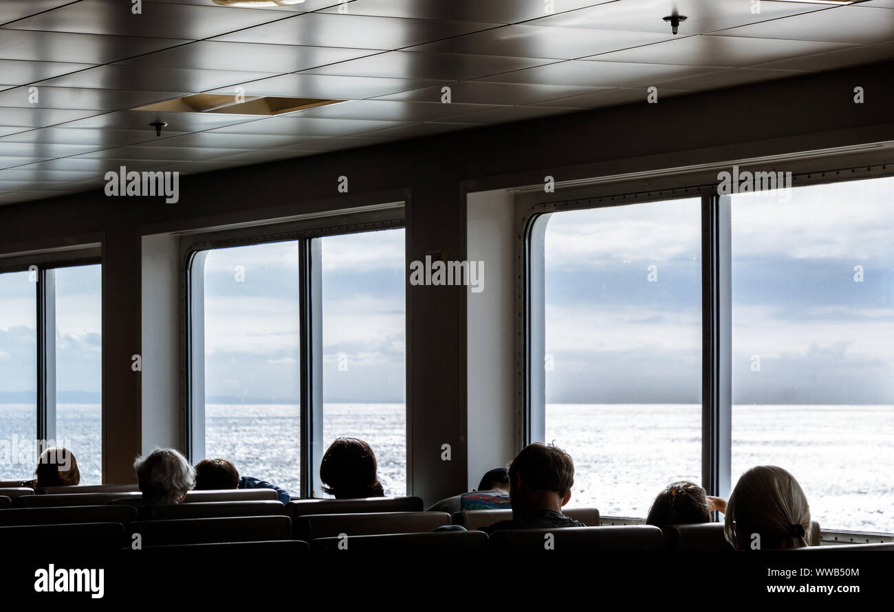Silhouettes of indoor boat passengers seated beside window looking ...