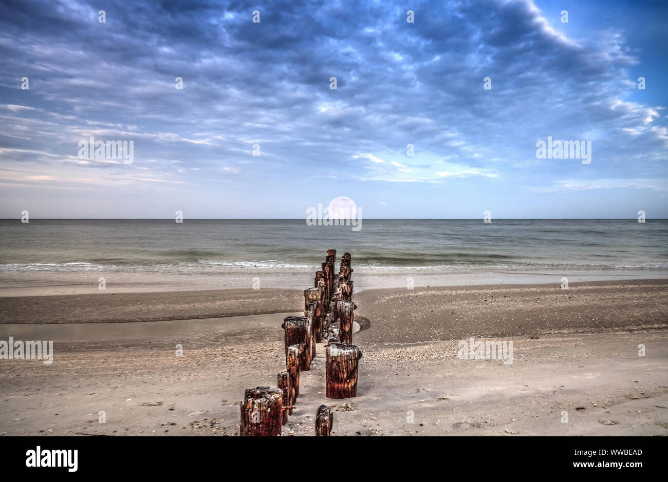 Moon set over an old pier in the ocean at Port Royal Beach at sunrise ...