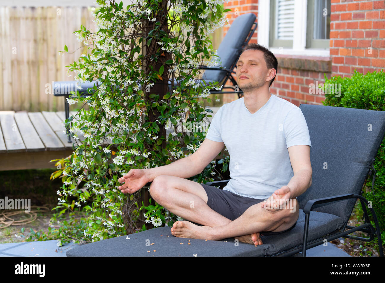 Young man sitting meditating on patio lounge chair with eyes closed in ...