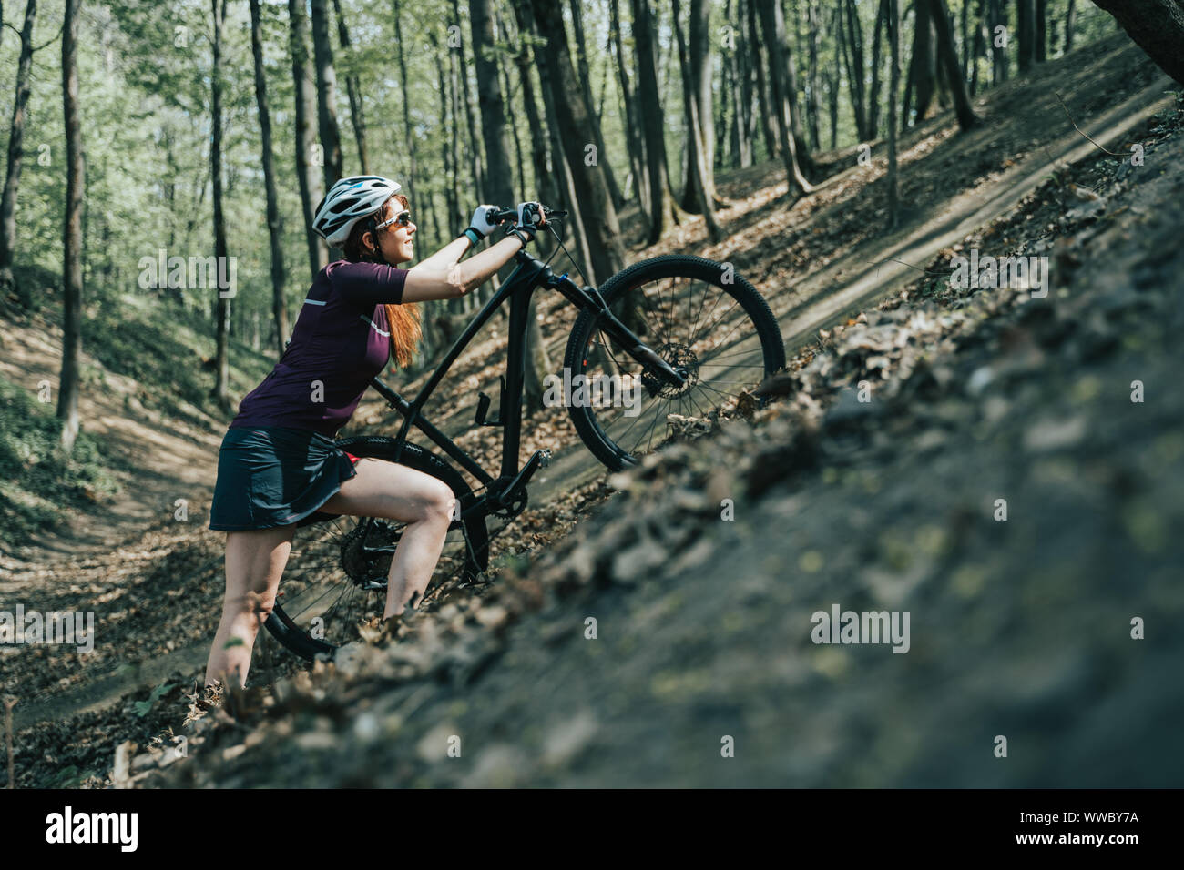 Photo of female athlete in helmet raising bicycle to hill in forest on ...