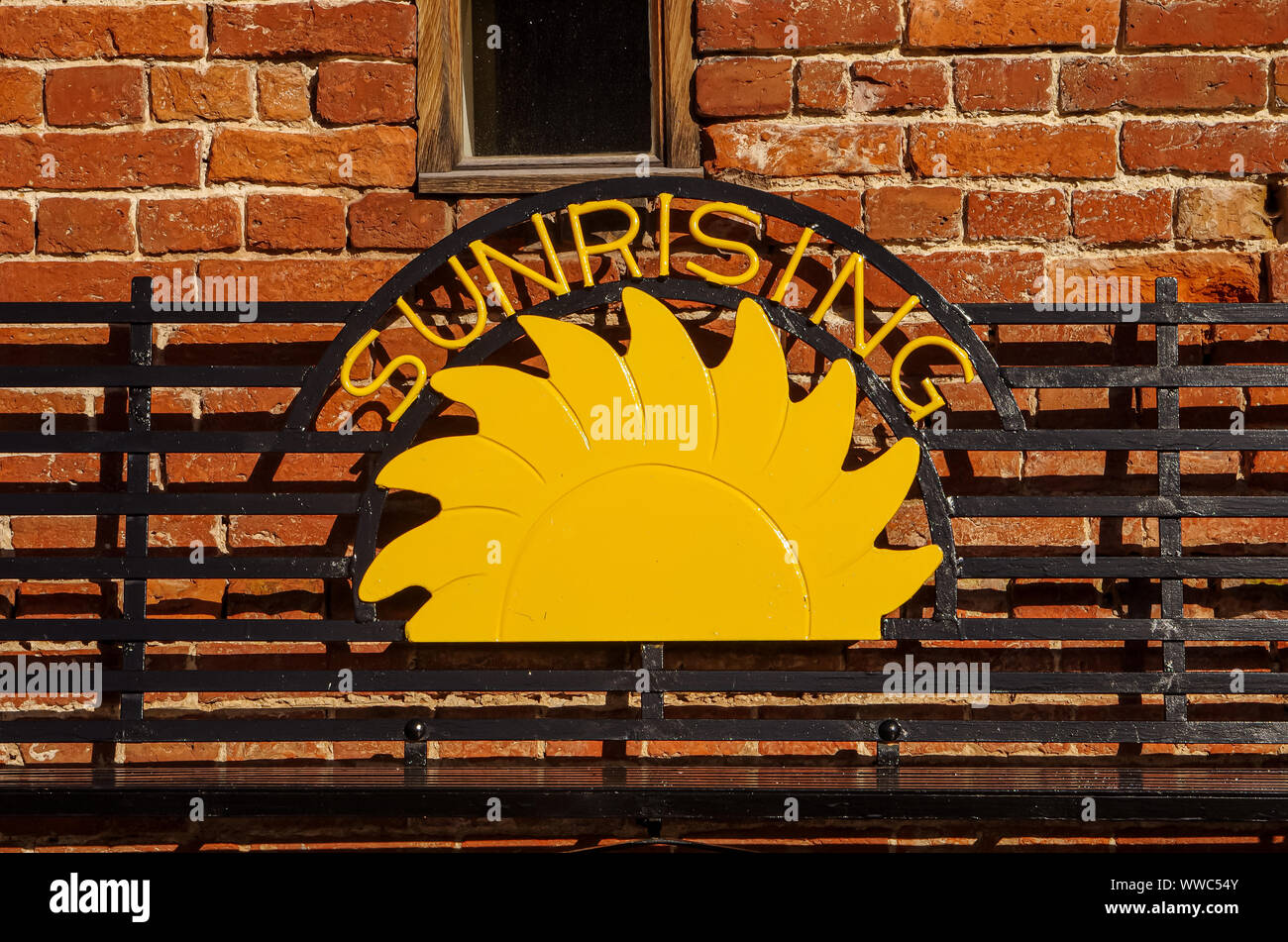 Sunrising sign in metal bench in front of red brick wall Stock Photo ...