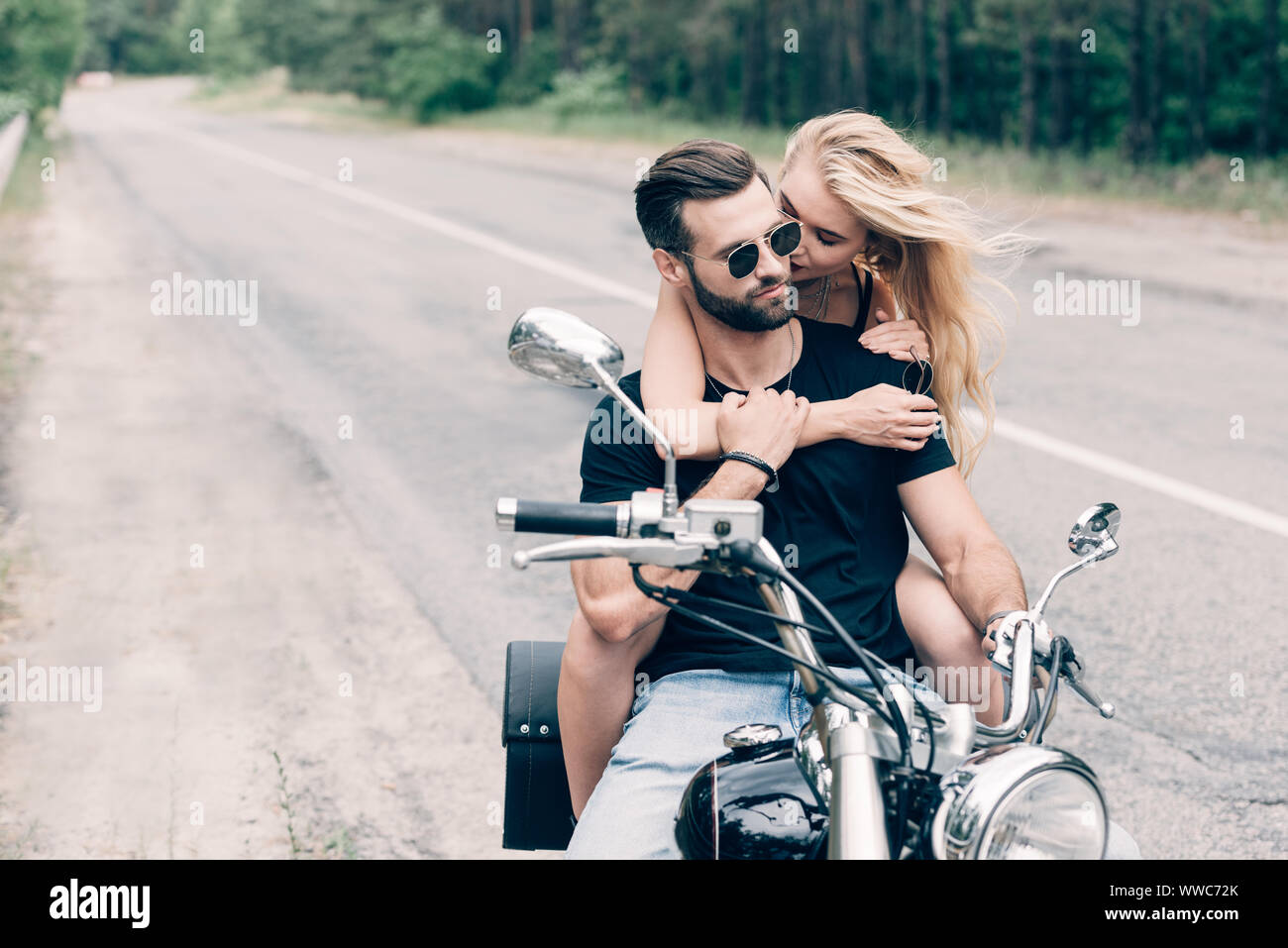 young tender couple of bikers hugging on black motorcycle on road near ...