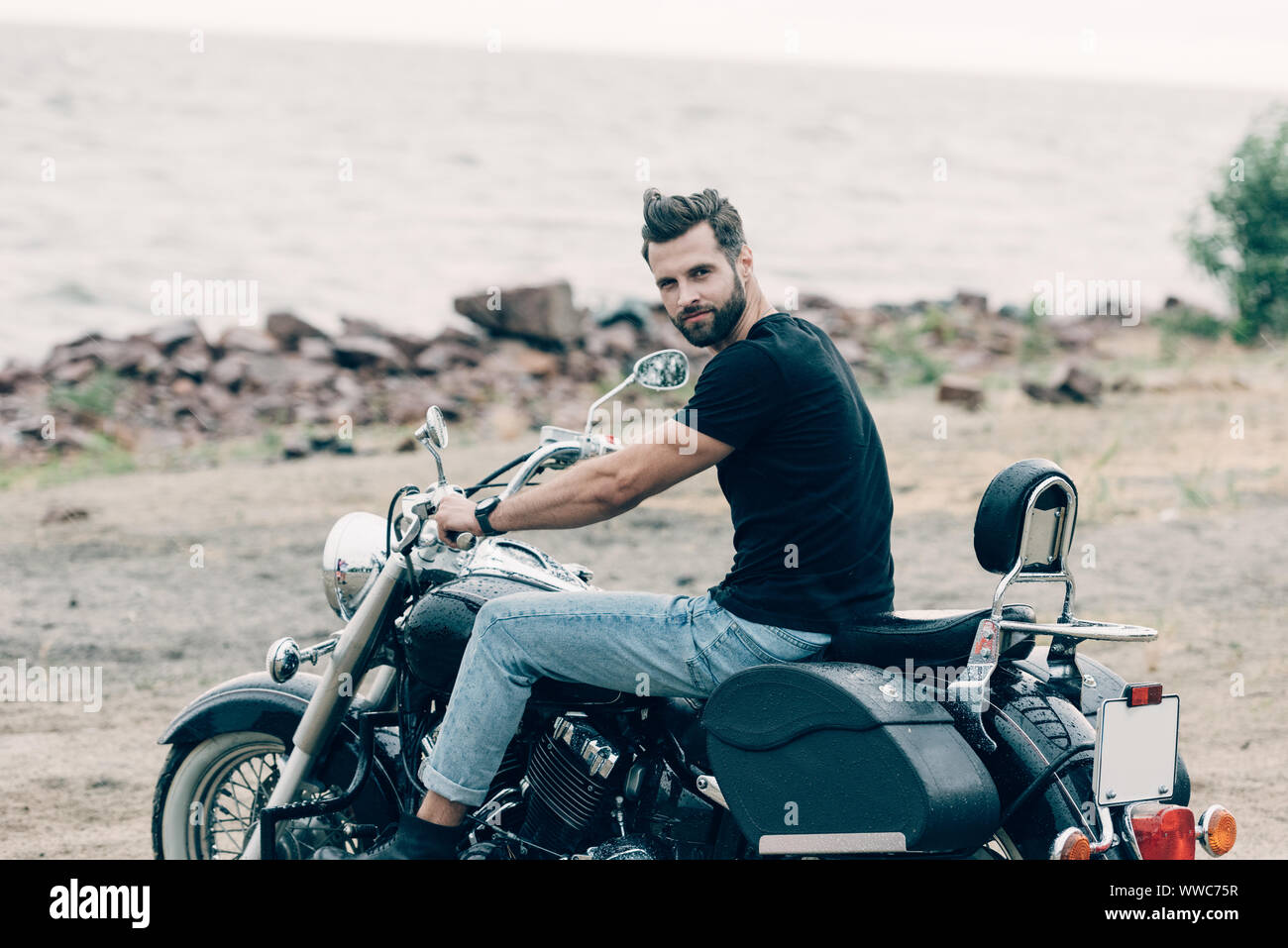 handsome bearded motorcyclist on black motorcycle at sandy beach near ...