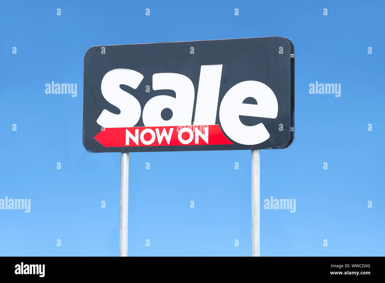 Sale now on sign direction arrow to shop against blue plain sky ...