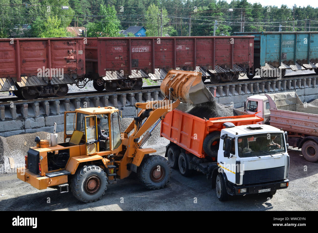 Wheel loader loads gravel into a dump truck at a cargo railway station ...