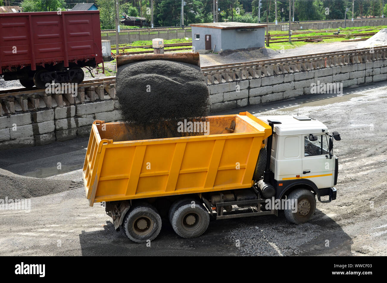 Wheel loader loads gravel into a dump truck at a cargo railway station ...