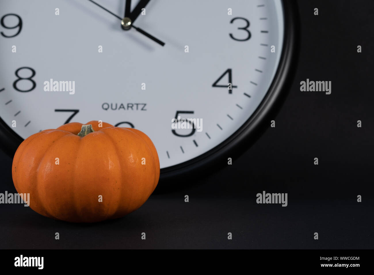 Mini pumpkin in foreground with big white clock, showing its time for ...