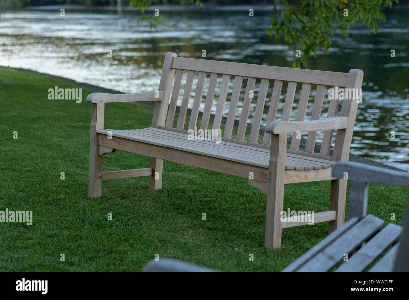 Two wooden benches in ninety degree angle on green grass at a shoreline ...