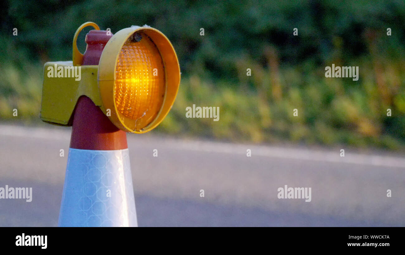 roadworks cone flashing on UK motorway at night with traffic passing ...