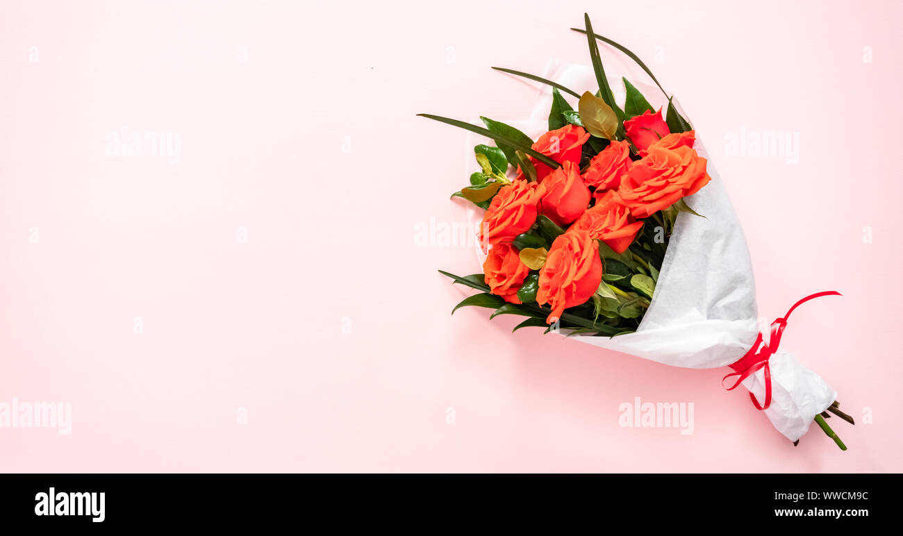 Flat lay. Bouquet of red roses and green leaves on a pink background ...