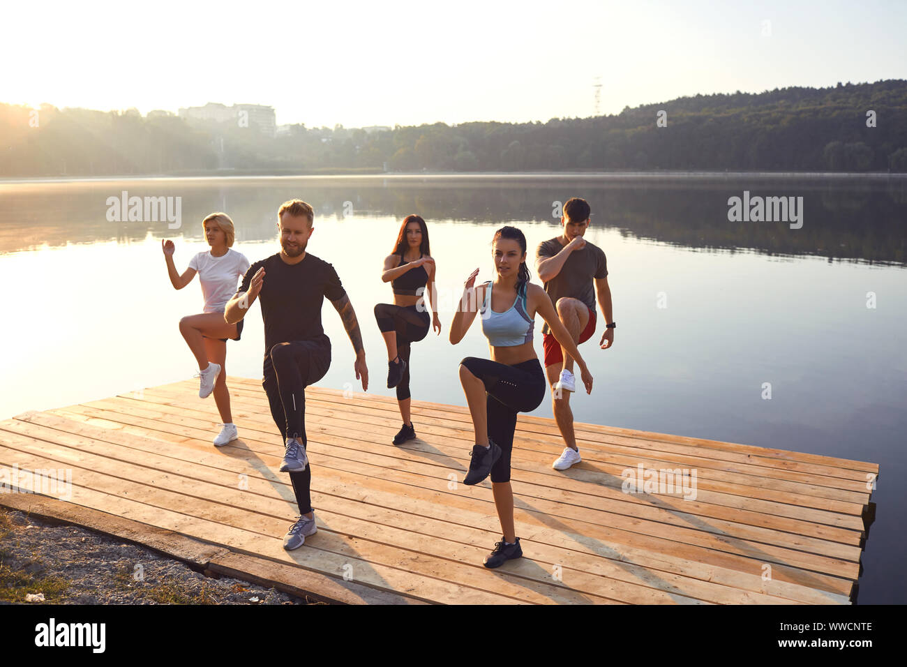 A group of active people do exercises in the park near the lake Stock ...