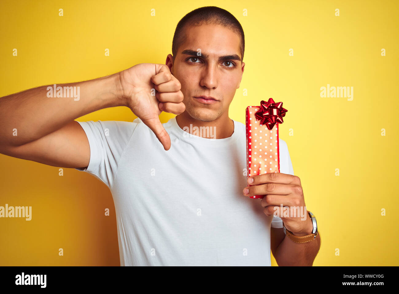 Young caucasian man holding birthday present over yellow isolated ...