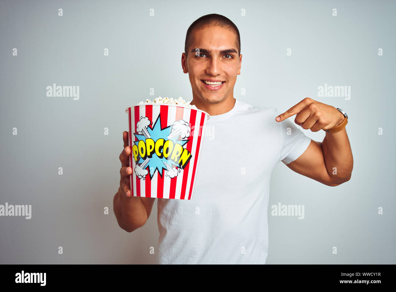 Young handsome man eating popcorn over white isolated background with ...